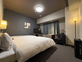 Quarto de hotel com uma cama grande, uma escrivaninha com cadeira, uma televisão de tela plana e uma luminária no teto.