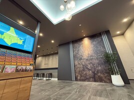 Um lobby de hotel moderno com um painel digital de mapa, um balcão de recepç ão e um grande mural na parede.