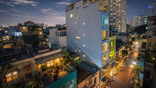 Vista urbana noturna com edifícios modernos, um jardim no terraço e uma rua movimentada abaixo.