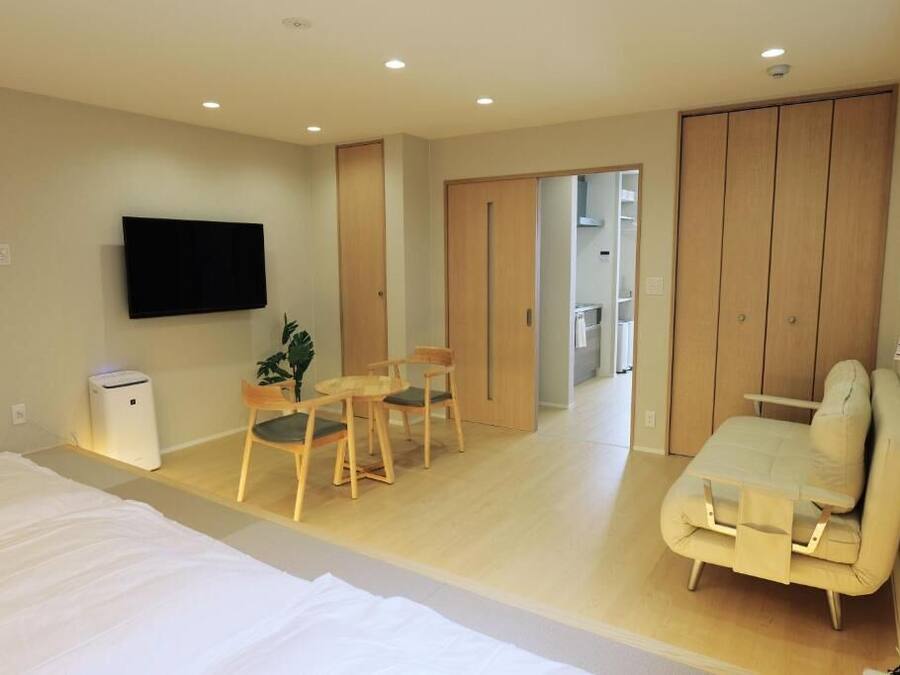 Quarto de hotel com cama, televisão, secretária com cadeiras, sofá e guarda-roupa.