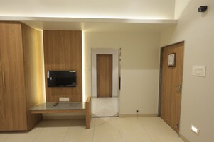 Quarto com armários de madeira, um banco embutido, televisão de tela plana e uma porta com um aviso.