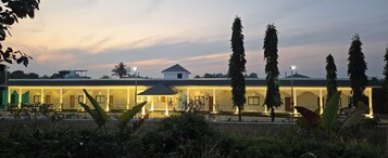 Um hotel com área externa coberta, um pequeno edifício e árvores altas.