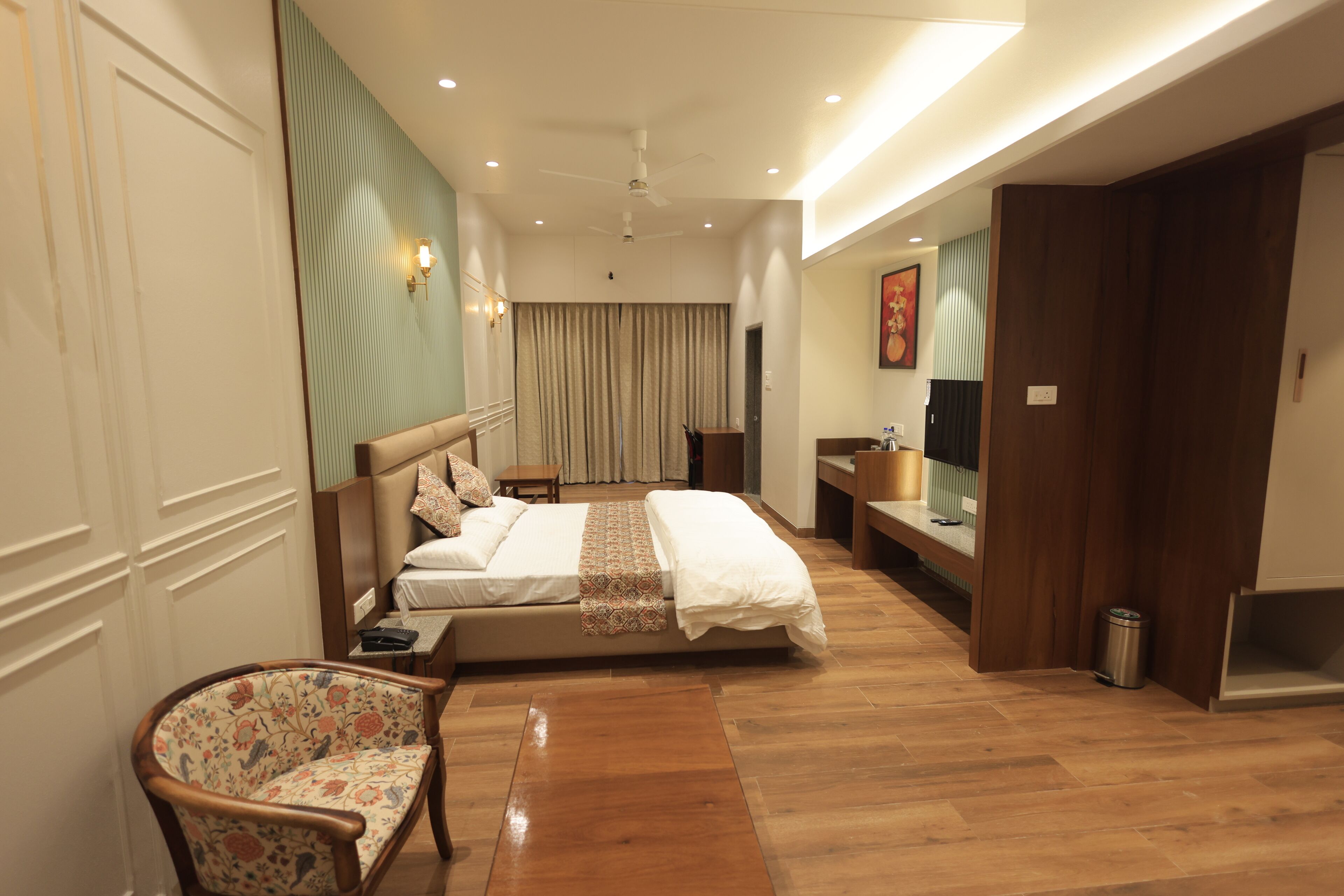 Quarto de hotel moderno com uma cama grande, piso de madeira, uma cadeira e uma escrivaninha com abajur.
