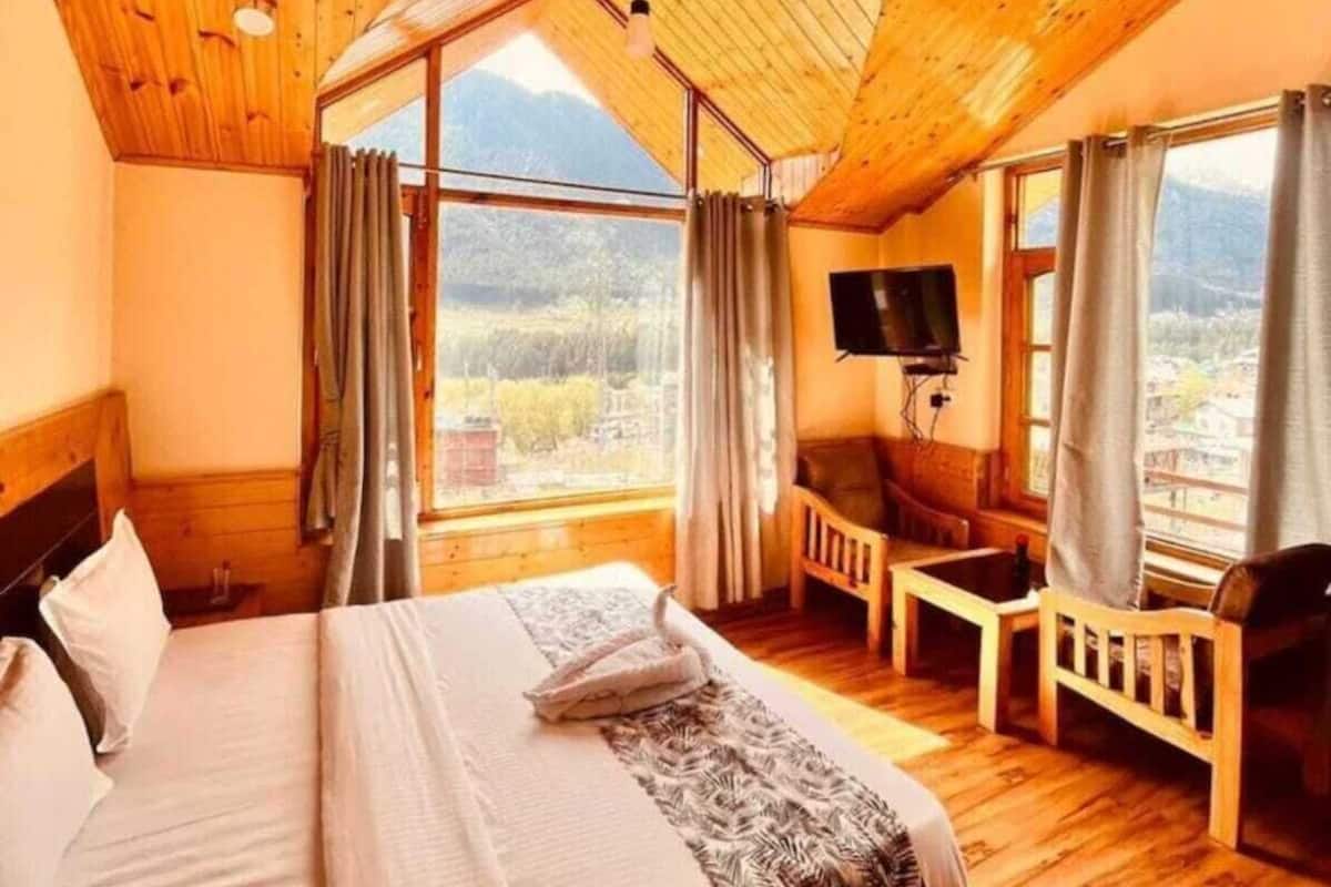 Quarto de madeira com uma cama, televisão e vista para as montanhas.