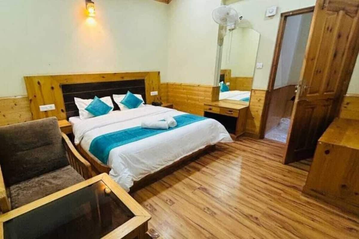 Quarto com estrutura de madeira, com cama, poltrona, mesa de cabeceira e espelho.