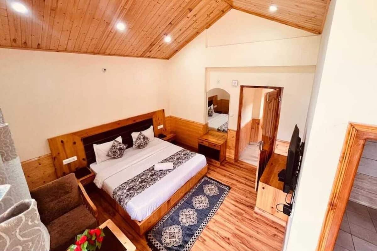 Um quarto com teto de madeira, cama com roupa de cama estampada, uma mesa pequena e uma cadeira.
