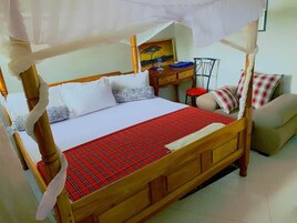 Uma cama de madeira com colcha xadrez vermelha e branca, uma mesa de cabeceira de madeira, uma cadeira e um sofá com almofadas estampadas.