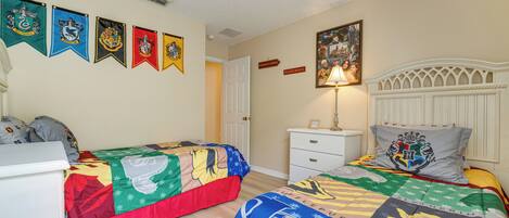 Quarto com duas camas, cômoda branca, mesa de cabeceira e parede decorada com bandeiras.