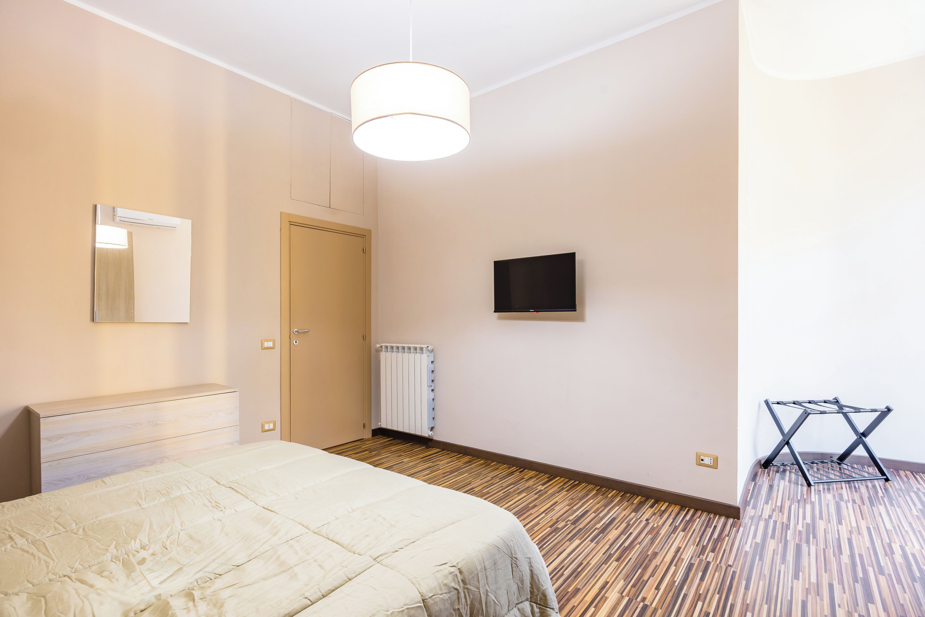 Quarto com cama, espelho, televisão e radiador.
