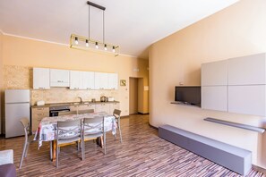 Uma cozinha moderna com armários brancos, uma mesa de jantar com cadeiras e uma TV de tela plana na parede.