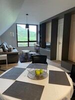 Sala de estar moderna com área de jantar, uma janela ampla com vista para campos verdes e teto estilo loft.