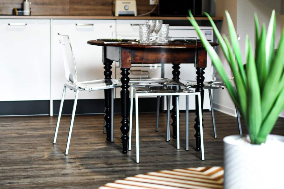 Uma cozinha moderna com armários brancos, uma mesa de jantar de madeira e um vaso com planta.