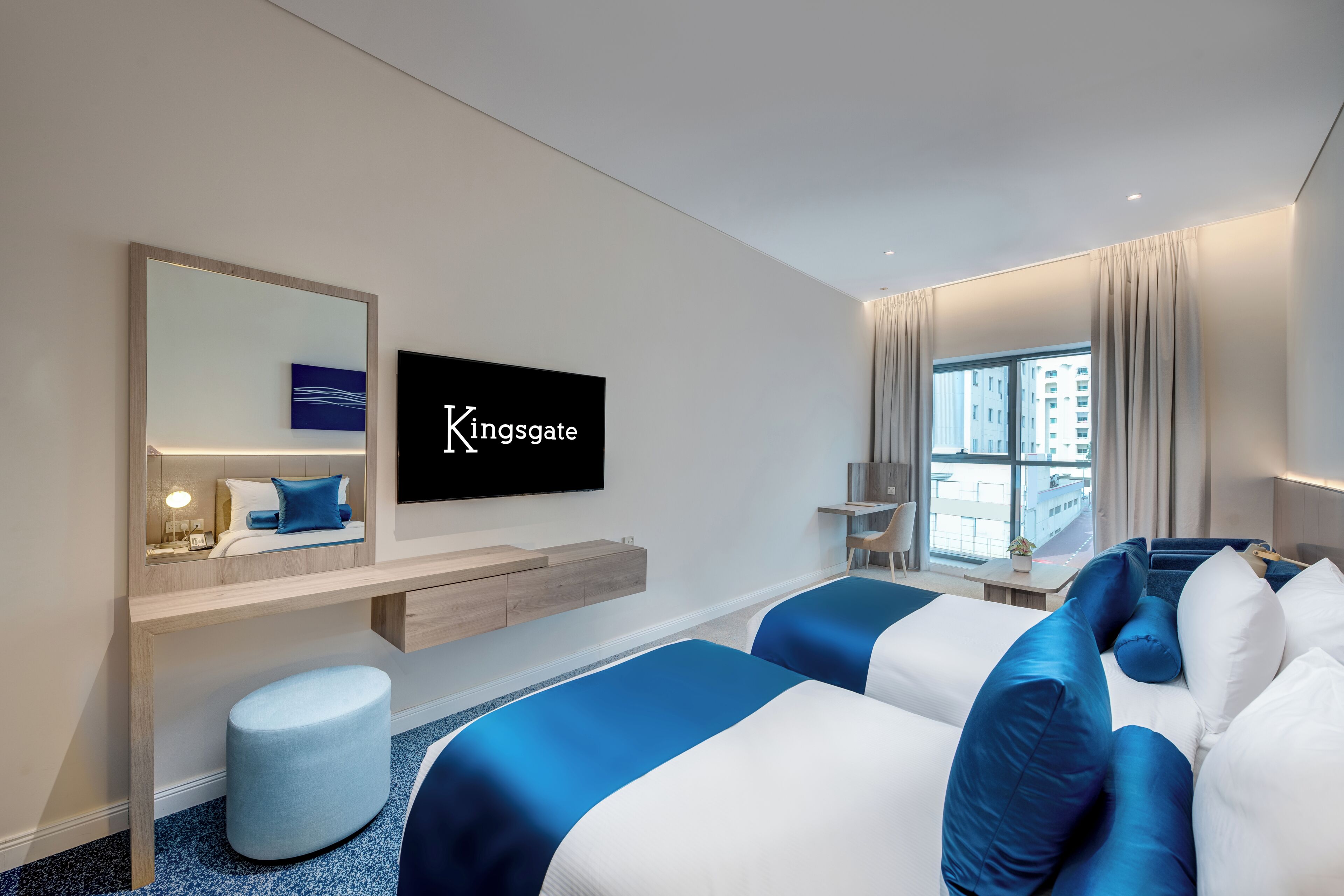 Quarto de hotel com televisão, escrivaninha, cadeira, cama e janela.