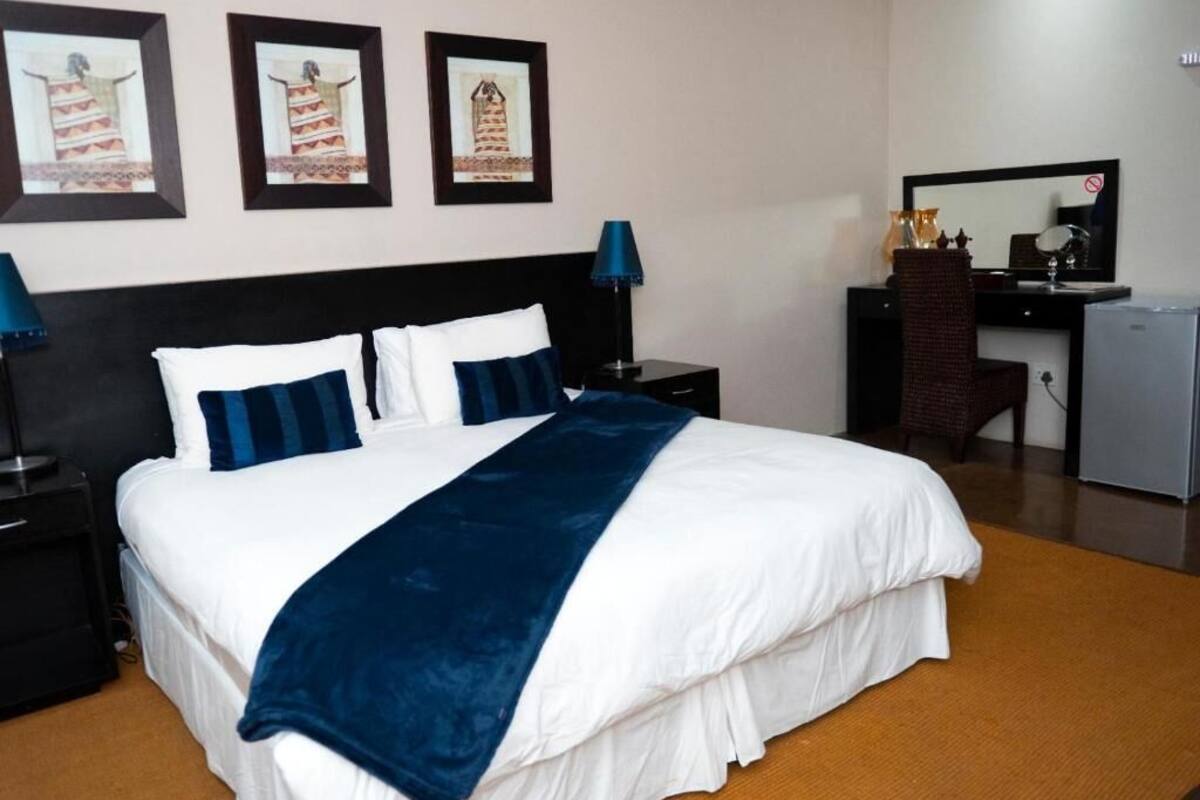 Quarto de hotel com uma cama grande, uma escrivaninha, uma cadeira e um espelho. Há quadros nas paredes.