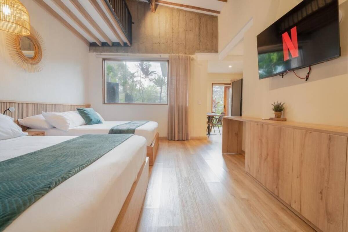 Quarto de hotel com duas camas, uma janela grande, teto de madeira e sinal da Netflix na parede.