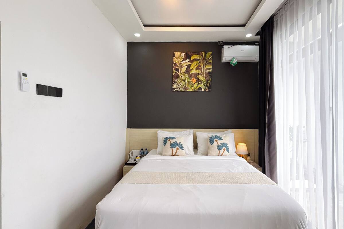 Quarto de hotel com cama, mesa de cabeceira, abajur e ar condicionado fixado na parede.