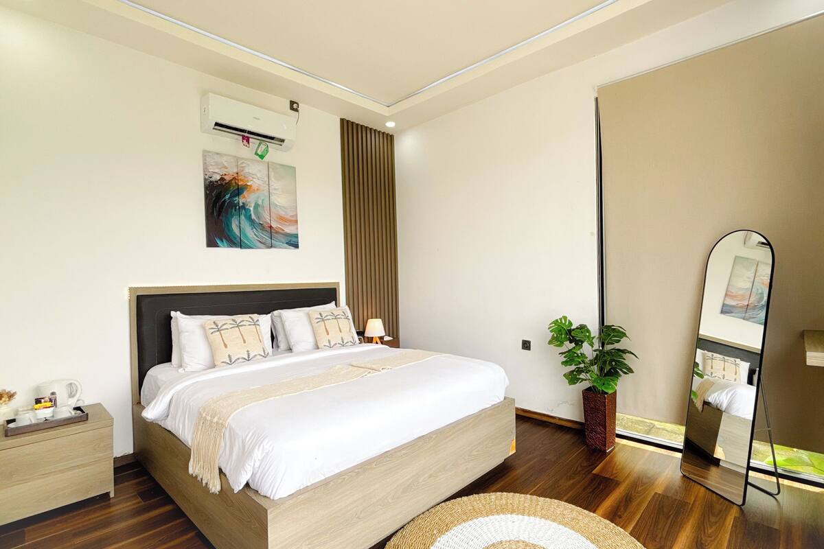 Quarto moderno com cama de madeira, mesa de cabeceira, planta em vaso e um espelho grande.