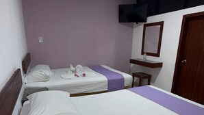 Quarto com duas camas, cabeceira de madeira, uma mesinha, um espelho e uma porta.