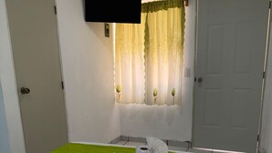 Quarto de hotel com uma cama, uma televisão fixada na parede e uma porta.