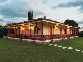 Uma casa de dois andares com fachada vermelha e branca, varanda coberta e gramado bem cuidado.