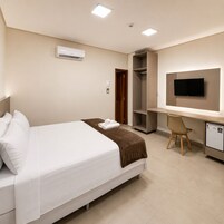 Quarto de hotel com uma cama, uma escrivaninha, uma cadeira, uma televisão e um guarda-roupa.