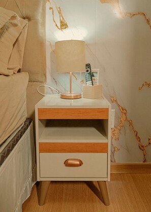 Uma mesinha de cabeceira com uma luminária, um controle remoto e uma gavetinha.