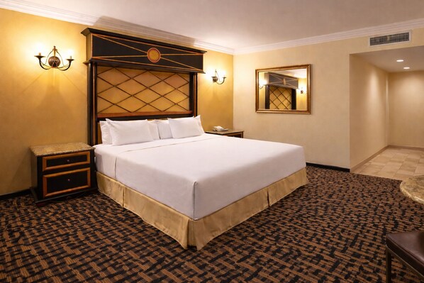 Quarto de hotel com cama grande, mesa de cabeceira e luminária fixa na parede, além de um espelho.