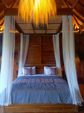 Uma cama de madeira com dossel, um cobreleito estampado e almofadas.