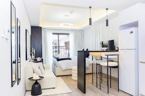 Quarto de hotel moderno com sofá, área de jantar, cozinha e varanda com vista.