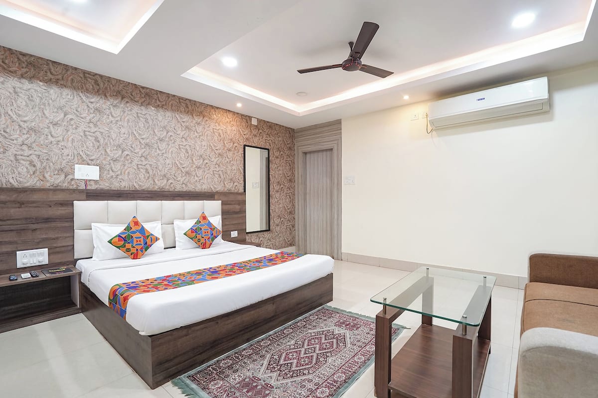 Quarto de hotel moderno com uma cama grande, uma mesa de centro de vidro, um ventilador de teto e um aparelho de ar condicionado.