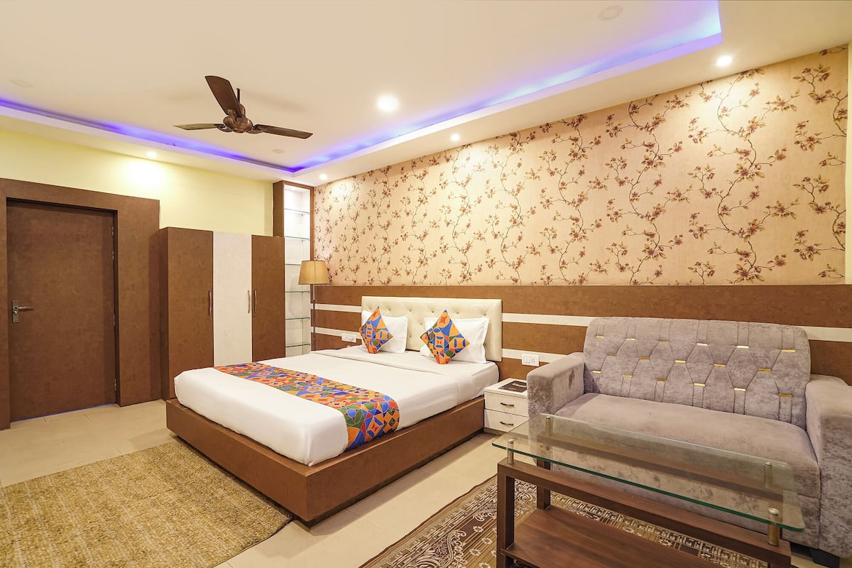 Quarto de hotel moderno com cama, sofá, mesinha de centro de vidro e ventilador de teto.