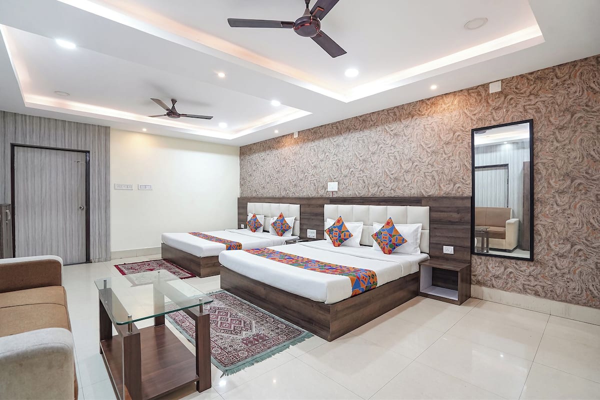 Quarto de hotel moderno com uma cama grande, duas mesas de cabeceira, uma mesa de centro de vidro, um sofá, um ventilador de teto e um espelho grande.