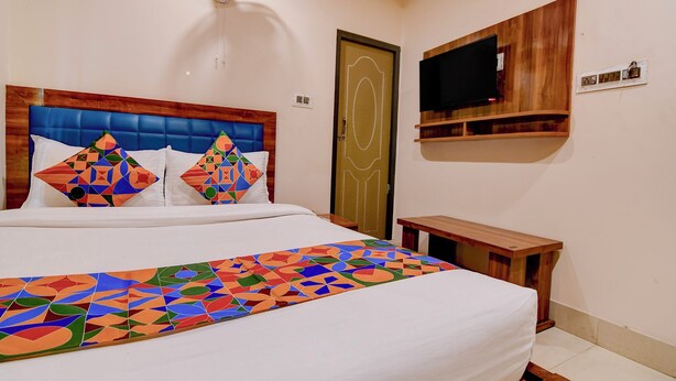 Quarto com cama, cabeceira de madeira, televisão presa à parede e mesa de cabeceira.