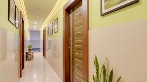 Corredor de hotel com porta de madeira com a placa “302”, plantas em vasos e quadros nas paredes.