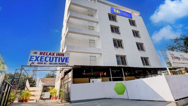 Um edifício de vários andares com uma placa indicando 'fab HOTELS' e 'RELAX INN EXECUTIVE', mostrando que oferece diversos tipos de quartos, incluindo com ar condicionado, sem ar condicionado e quartos deluxe.