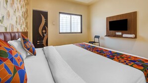 Quarto de hotel com uma cama grande, uma televisão fixada na parede, uma janela e uma porta com detalhes decorativos.