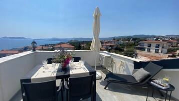 Terraço no telhado com uma mesa posta para dois, uma cadeira de lounge e um ventilador.