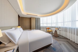 Quarto de hotel moderno com uma cama grande, uma pequena mesa e uma cadeira.