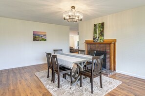 Uma sala de jantar com mesa de madeira, cadeiras, lustre e lareira.