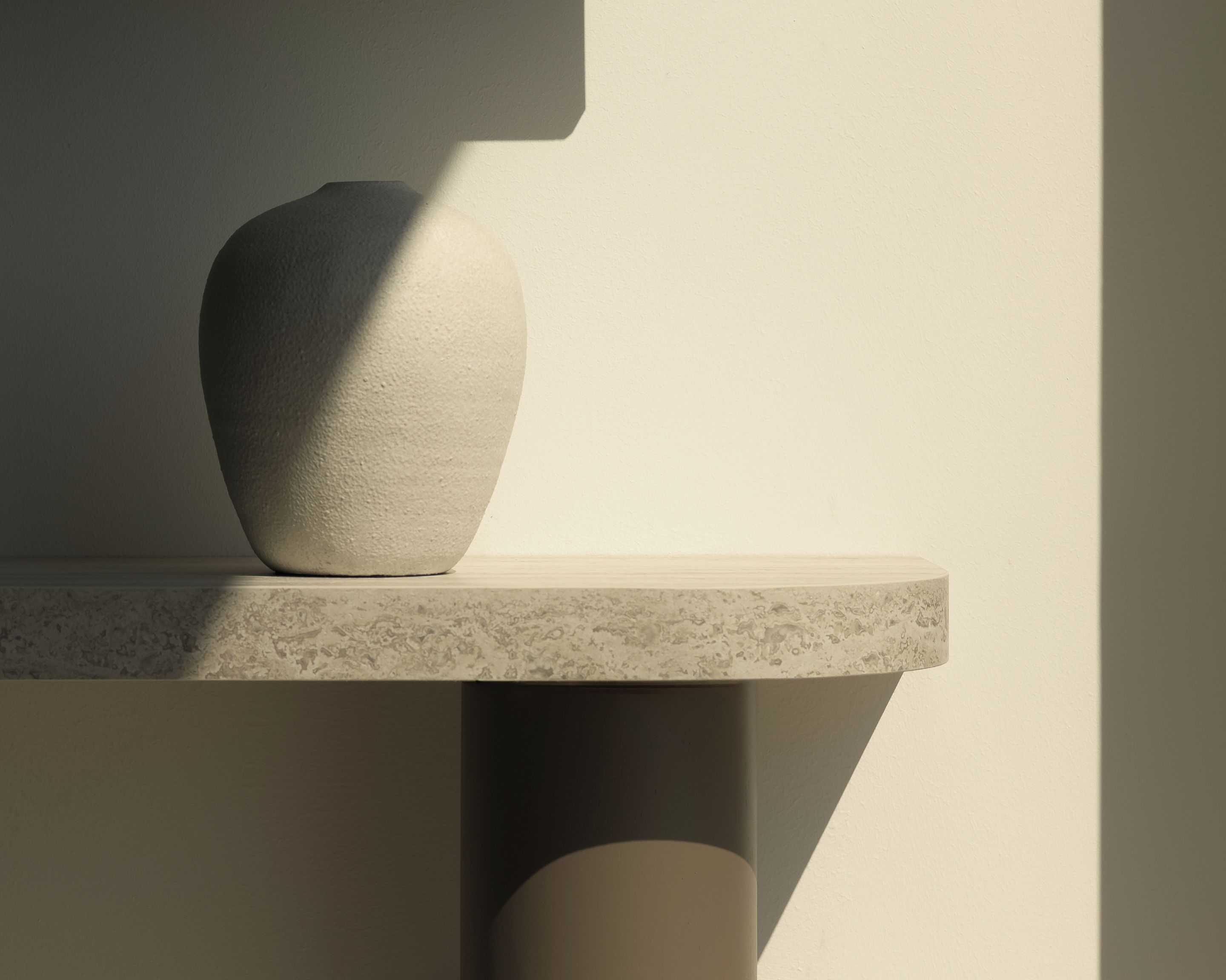 Vaso de pedra minimalista sobre superfície plana, com sombra projetada na parede.