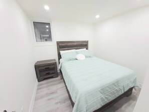 Quarto com cama, mesa de cabeceira, janela e luminária no teto.