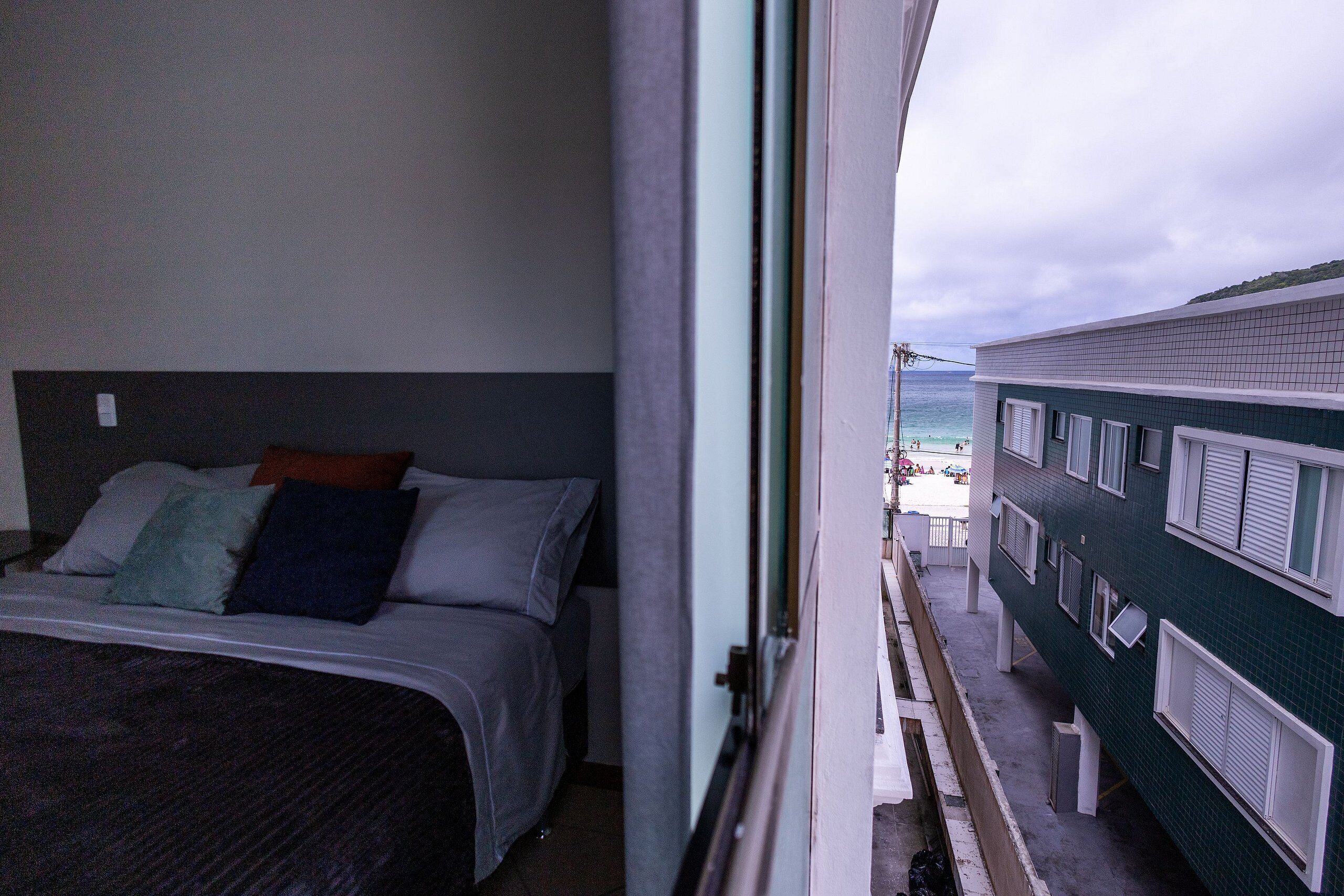 Quarto de hotel com cama, vista para a praia e um edifício com aparelhos de ar condicionado.