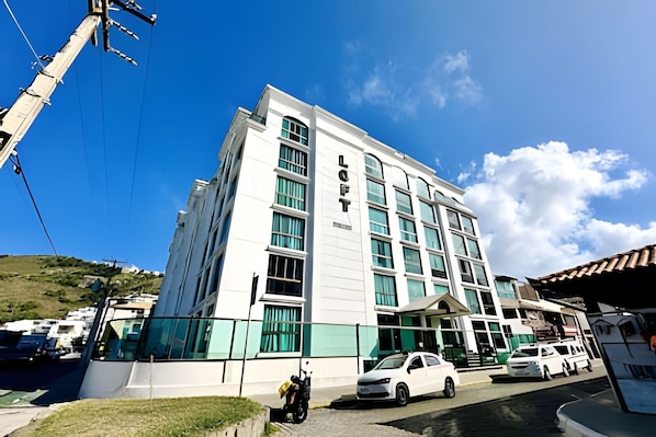 Um edifício de vários andares com um letreiro grande escrito 'LOFT', janelas amplas e um estacionamento com vários carros.