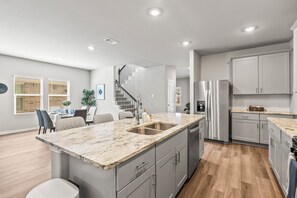 Cozinha moderna com ilha central, eletrodomésticos de aço inoxidável e área de refeições com escada que dá acesso a outro nível.