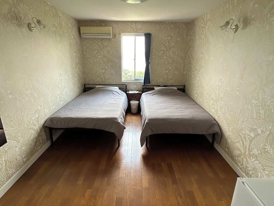 Quarto com duas camas, janela com cortinas, ar condicionado e piso de madeira.