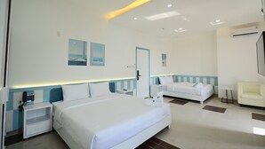 Quarto de hotel com uma cama grande, uma cama menor, uma escrivaninha, uma cadeira e um espelho.