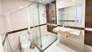 Uma casa de banho moderna com chuveiro envolto em vidro, sanita, lavatório e espelho.