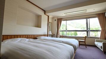Quarto de hotel com duas camas, janela com vista para o verde, uma cadeira e uma mesinha.