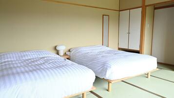 Quarto em estilo japonês tradicional com tatames, duas camas de solteiro com roupa de cama branca, uma mesa de cabeceira de madeira e um guarda-roupa com portas de correr.