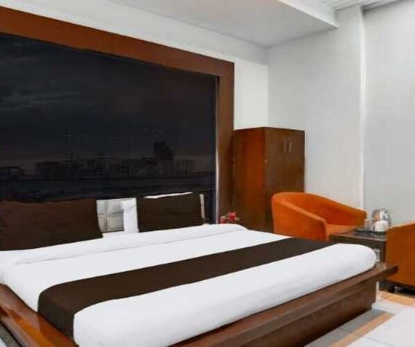 Quarto de hotel com uma cama grande, cabeceira de madeira, mesa de cabeceira, uma cadeira laranja e vista para um horizonte urbano pela janela.